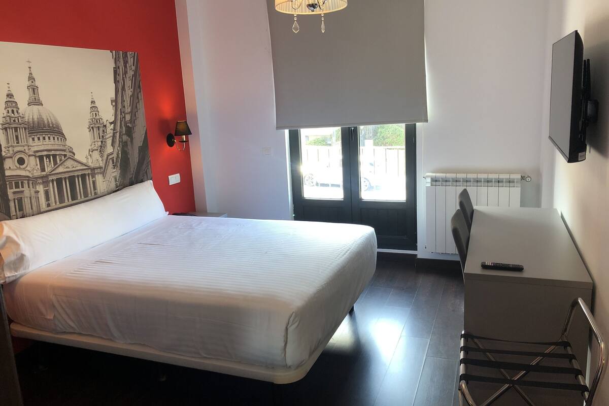 Quarto de hotel com uma cama grande, uma cadeira, uma TV, uma janela com vista para o exterior e um quadro na parede.