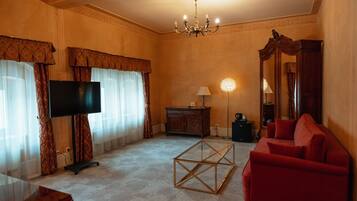Uma sala de estar com televisão, sofá vermelho, mesa de centro de vidro e um candelabro.