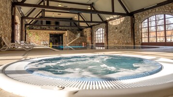 Uma banheira de hidromassagem numa área interna com piscina de paredes de pedra e vista para o exterior.