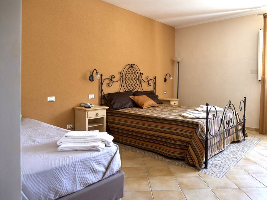 Um quarto com cama, mesa de cabeceira, abajur e janela com cortinas.