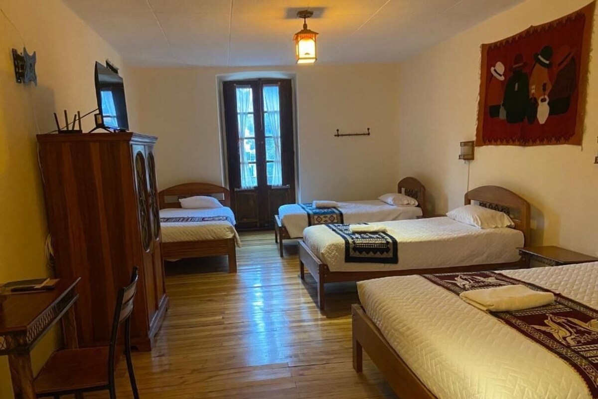 Quarto de hotel com duas camas, uma escrivaninha de madeira, uma cadeira e um guarda-roupa.