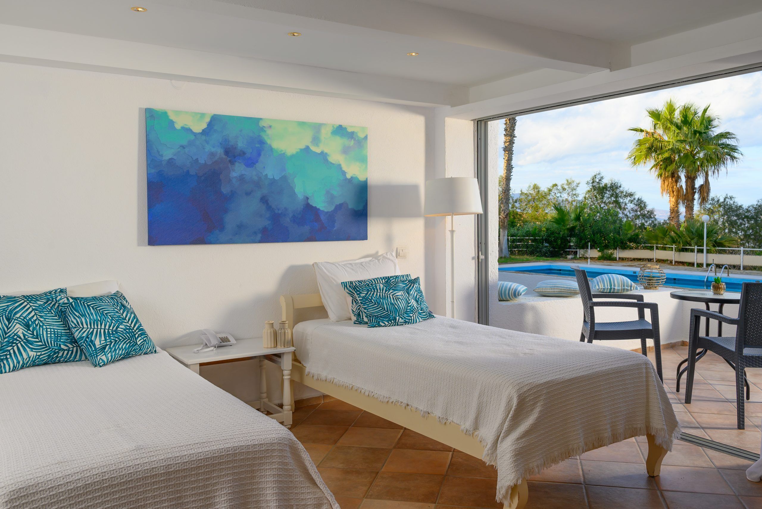 Quarto de hotel com duas camas, um quadro, um abajur, um telefone e vista para uma piscina.