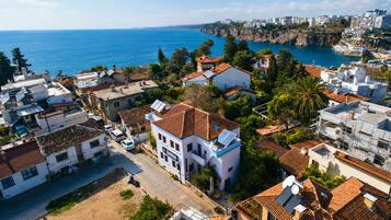 Zona residencial costeira com casas de telhado em terracota, um edifício branco de destaque com painéis solares e vista para o mar.