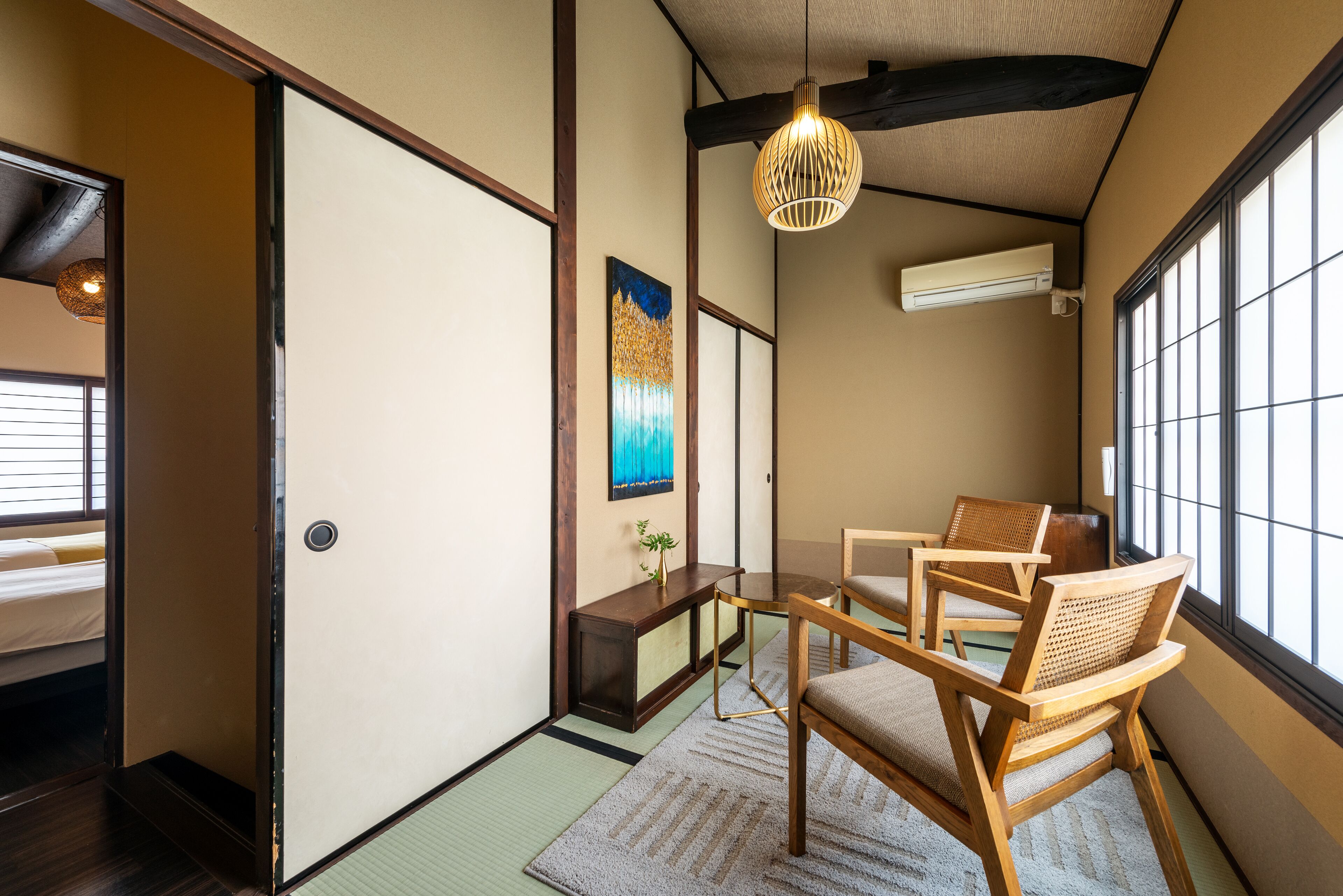 Um quarto japonês tradicional com tatames, uma mesa baixa com cadeiras, um candeeiro pendente e uma grande janela com vista.