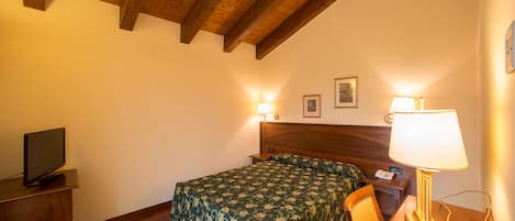 Quarto com cama, escrivaninha com abajur, cadeira e televisão sobre um aparador de madeira.
