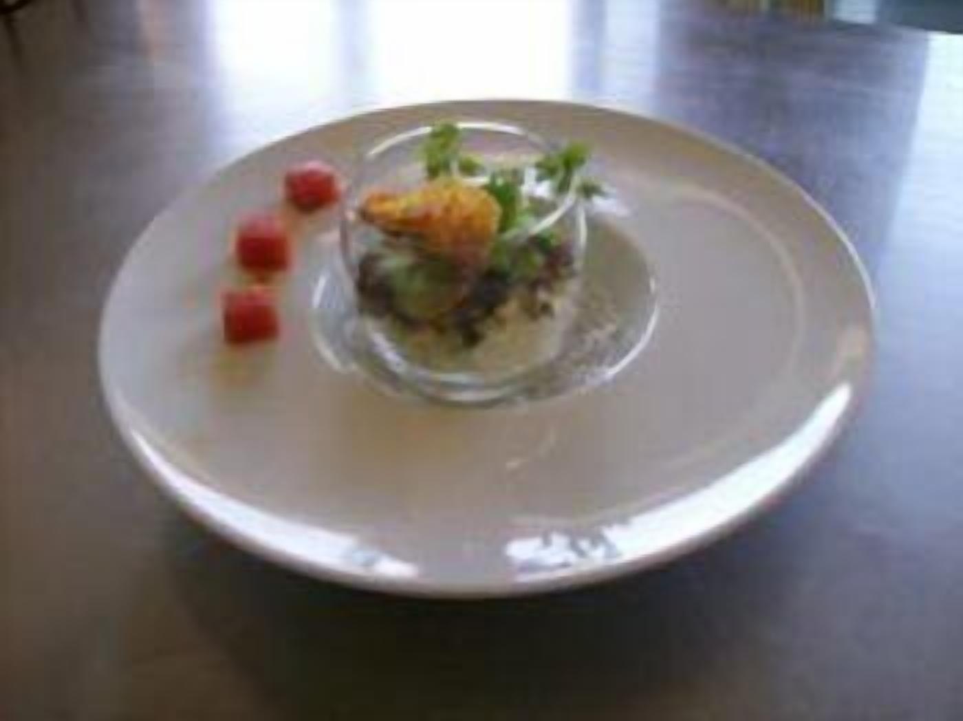 Um prato com uma pequena porção de comida, possivelmente uma salada ou entrada, sobre um prato branco.
