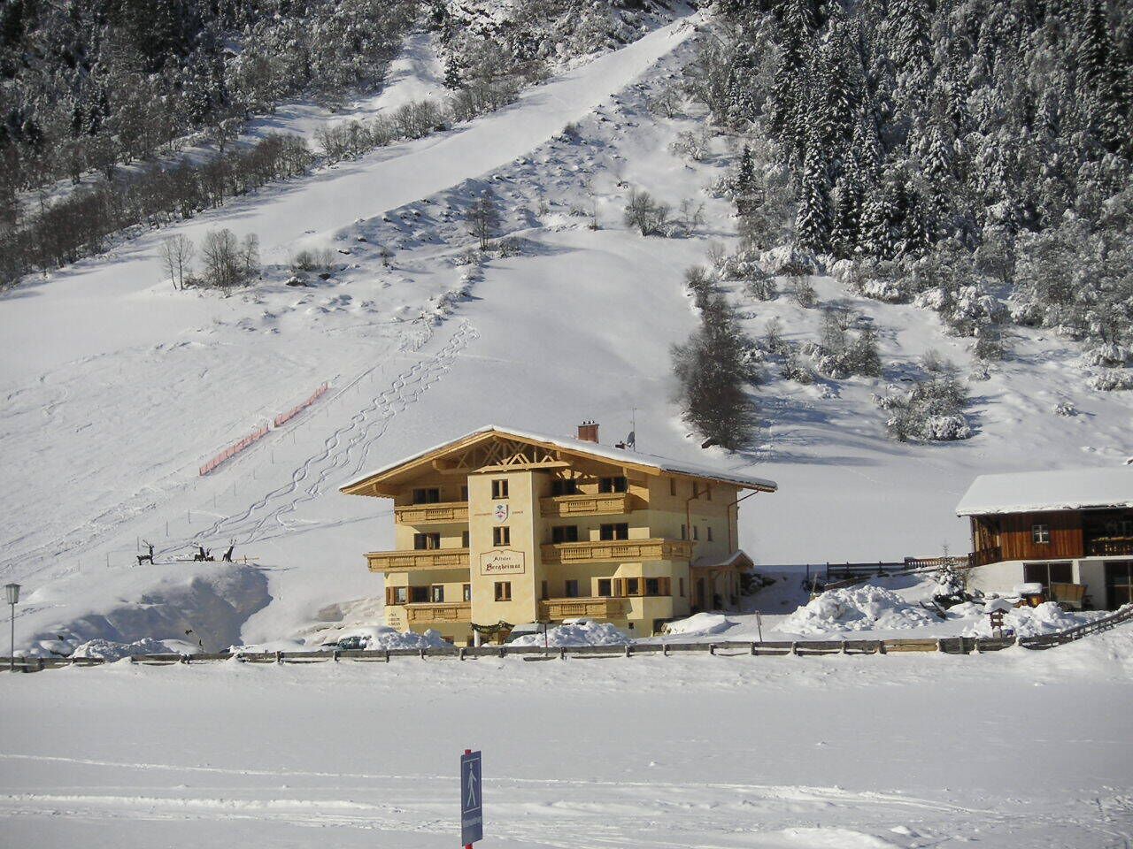 Um edifício de vários andares com um teleférico ao fundo, rodeado por árvores cobertas de neve e uma pista de esqui.