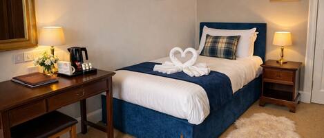 Quarto de hotel bem arrumado, com cama, mesas de cabeceira, escrivaninha e uma cadeira.