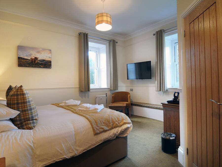 Quarto de hotel com uma cama, uma cadeira, uma escrivaninha, uma televisão e um quadro na parede.