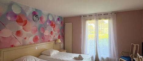 Quarto de hotel com duas camas, uma cadeira, uma janela com cortinas e uma parede com padrão floral.