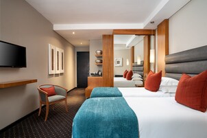 Quarto de hotel com uma cama grande, uma cadeira, uma televisão e uma escrivaninha com abajur.