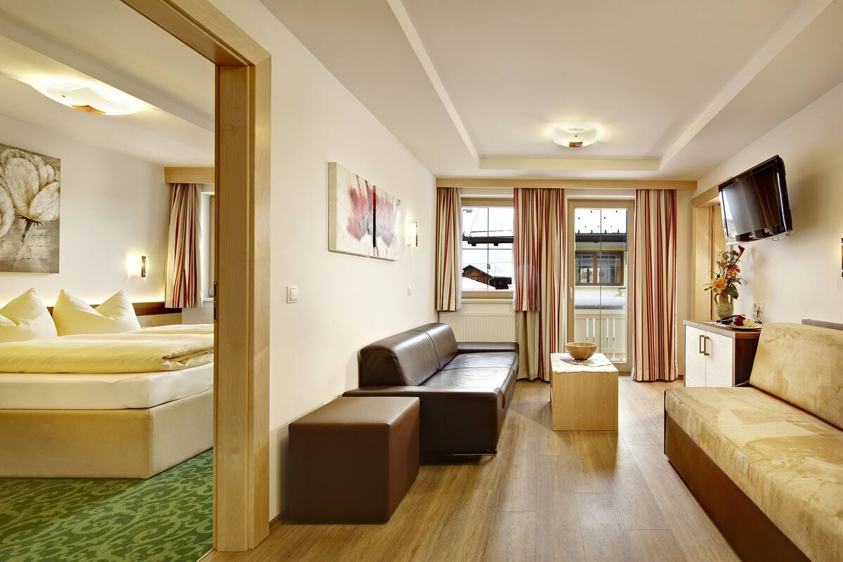 Quarto de hotel moderno com cama, sofá, televisão e janela com cortinas.