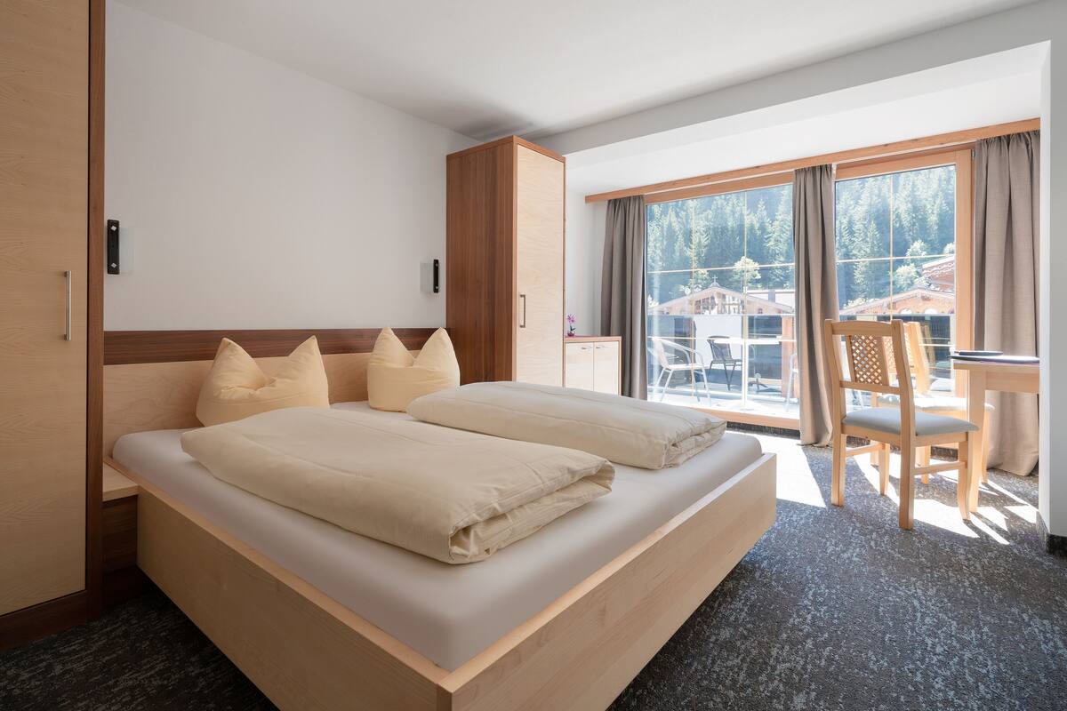 Quarto de hotel com uma cama grande, um guarda-roupa de madeira, uma escrivaninha e uma cadeira.