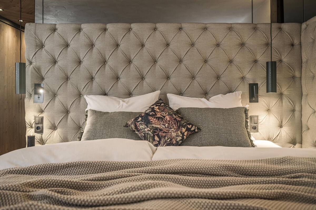 Quarto com cabeceira estofada, duas luminárias de apoio e almofada decorativa estampada.
