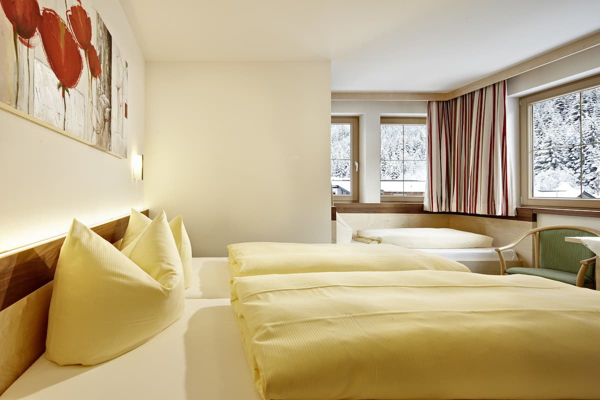 Quarto de hotel com duas camas, um painel de cabeceira de madeira, uma cadeira verde e uma janela com vista para árvores cobertas de neve.