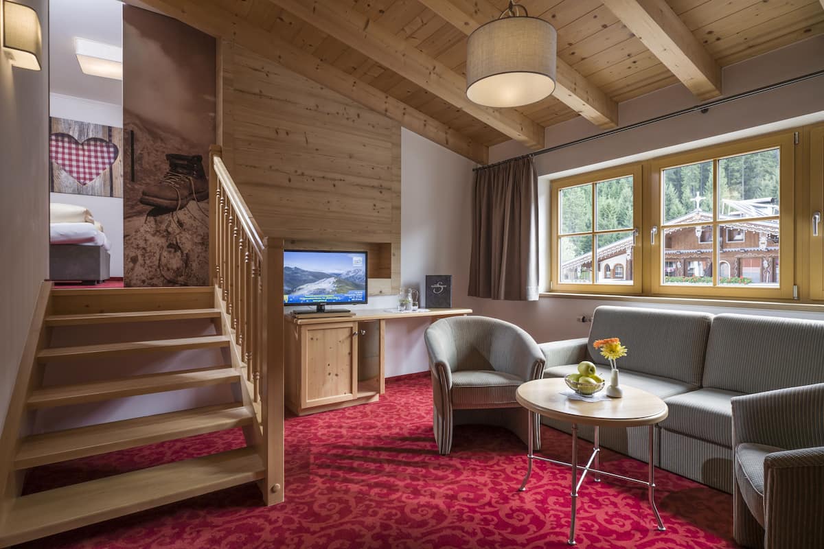 Quarto com escada de madeira, uma mesa com computador, sofá e janela com vista para uma montanha.