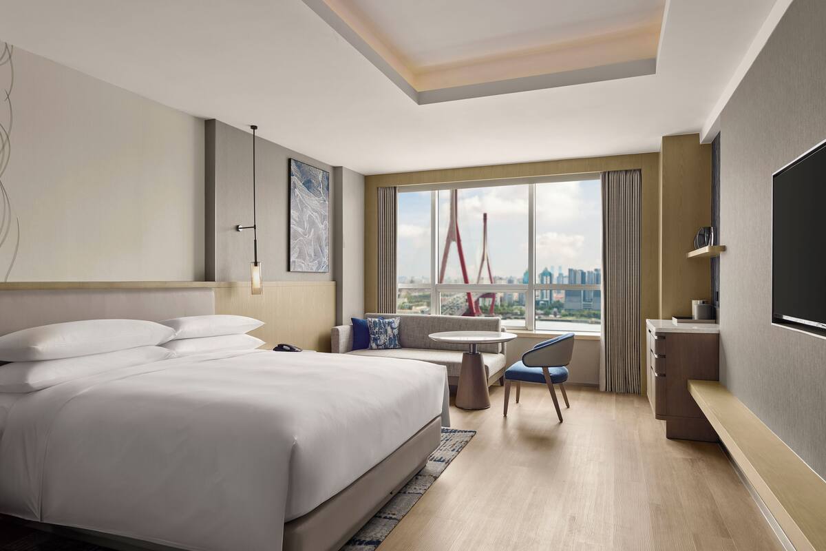 Quarto de hotel moderno com uma cama grande, uma escrivaninha, uma cadeira e uma televisão.
