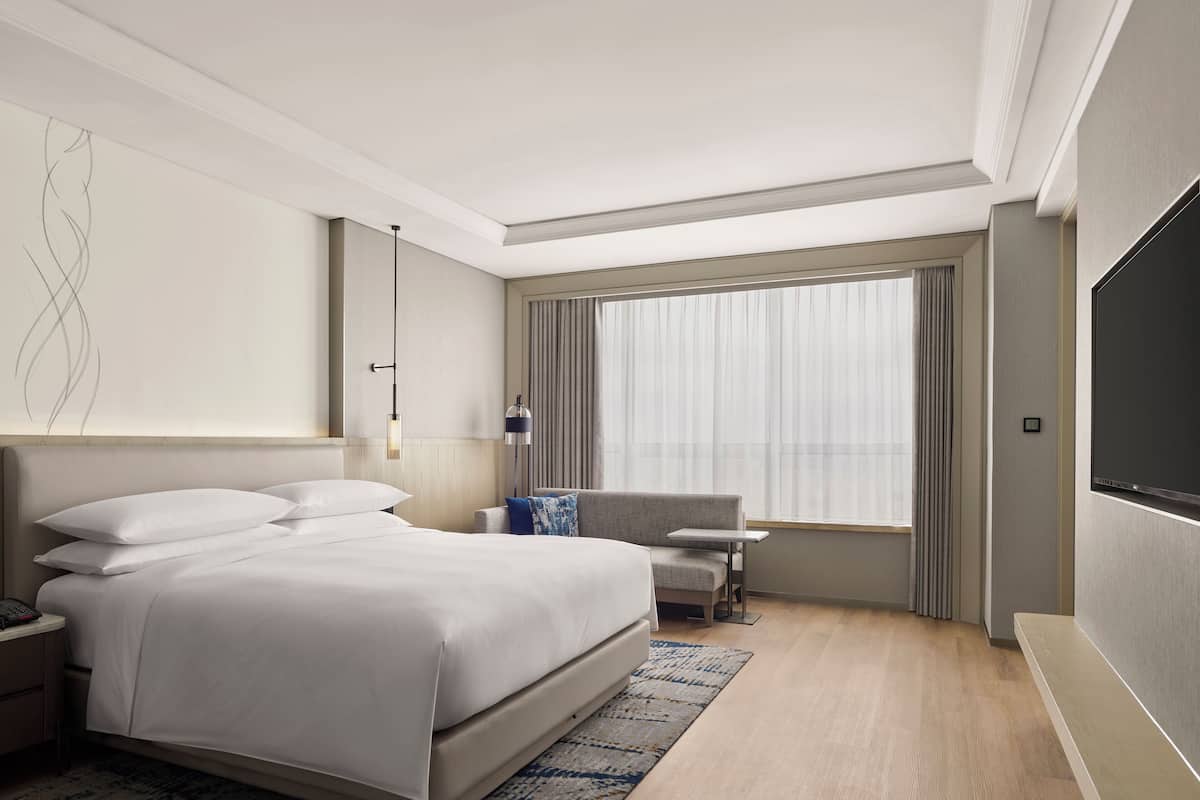 Quarto de hotel moderno com uma cama grande, uma mesa de trabalho, uma televisão e uma janela com cortinas.