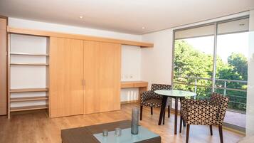 Quarto moderno com guarda-roupa de madeira, uma mesa redonda com cadeiras e uma janela grande com vista para árvores.