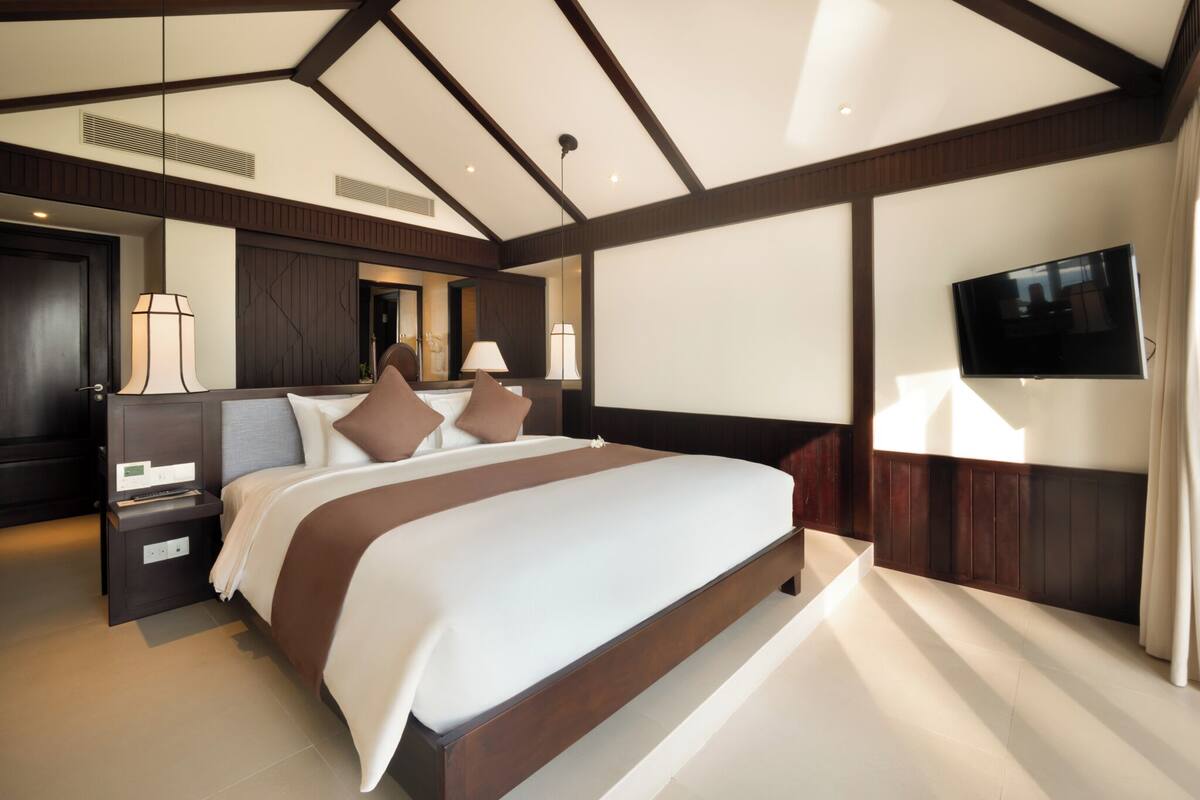 Quarto de hotel moderno com uma cama grande, televisão de tela plana, mesa de cabeceira e televisão fixada na parede.