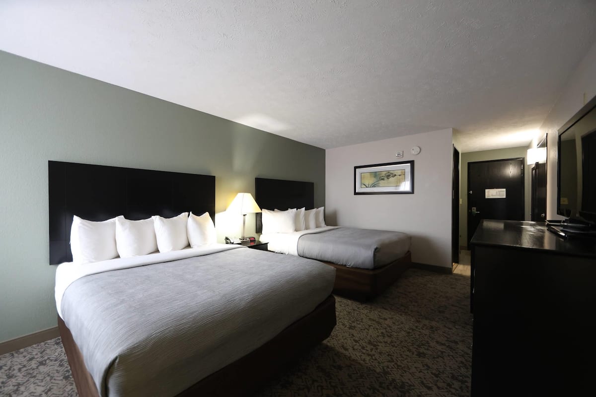 Quarto de hotel com duas camas, uma escrivaninha, um espelho e um quadro pendurado na parede.