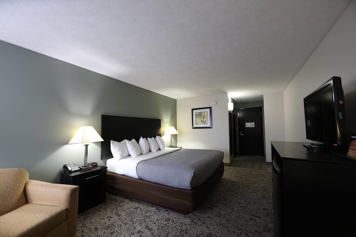 Quarto de hotel com cama, luminárias de cabeceira, televisão, escrivaninha e uma cadeira.