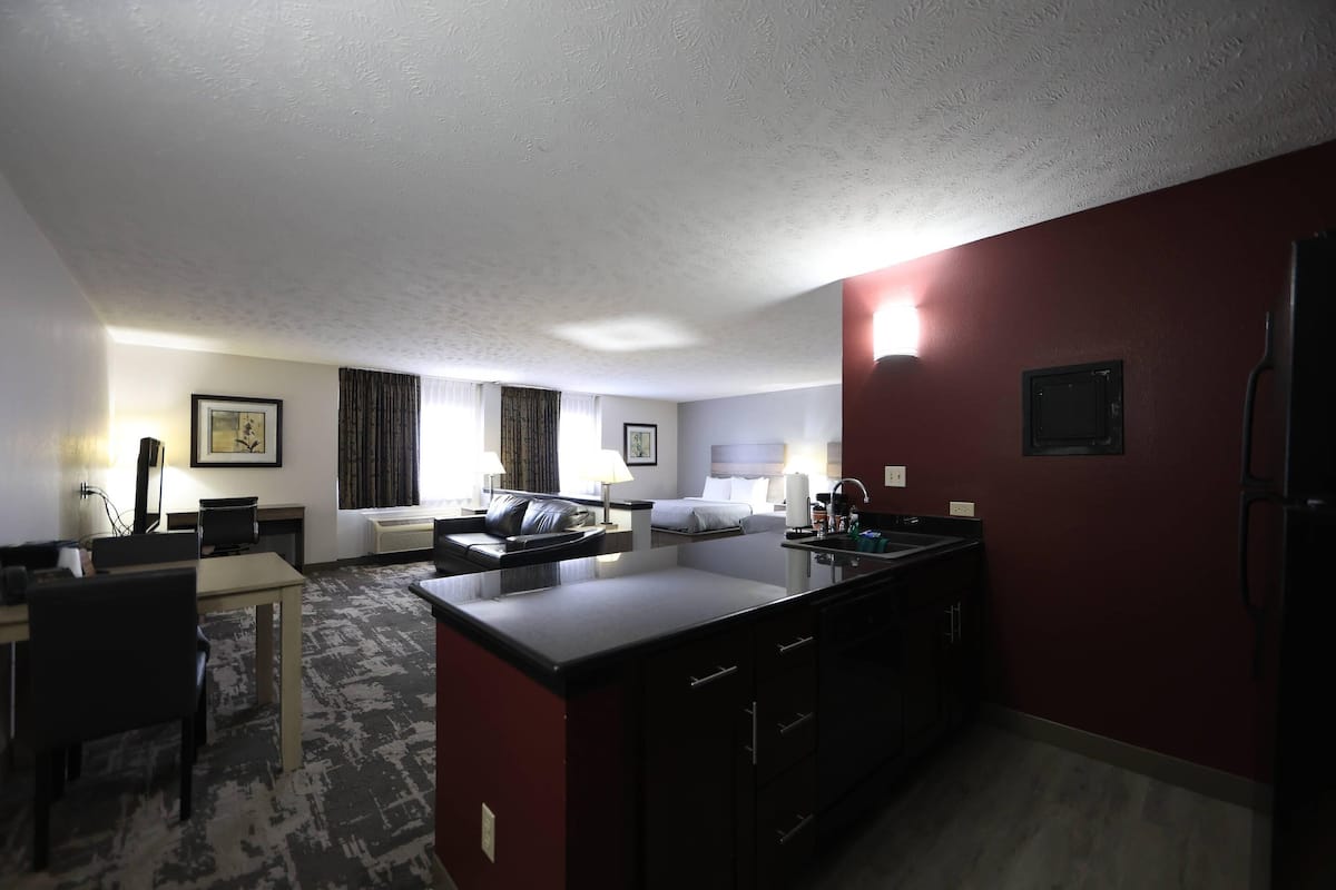 Quarto de hotel com cozinha compacta, área de refeições, cama e banheiro.