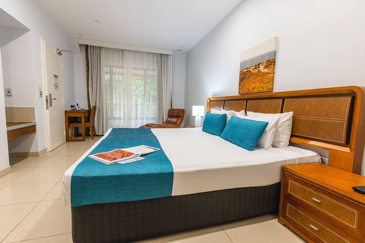 Quarto de hotel com uma cama grande, uma escrivaninha, uma cadeira e uma janela com cortinas.