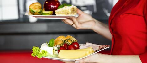 Uma pessoa segurando uma bandeja com diversos alimentos, incluindo sanduíche, maçã, queijo e vegetais.