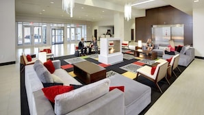 Um lobby espaçoso com design moderno, destacando uma área central de estar com sofás, poltronas, uma mesa de centro e uma lareira.