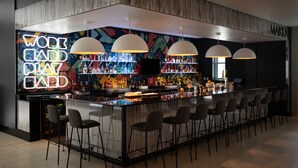 Uma área de bar com um balcão comprido, vários banquinhos e um mural colorido.