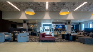 Um lobby moderno com teto estampado, diversas áreas de estar e um bar central.