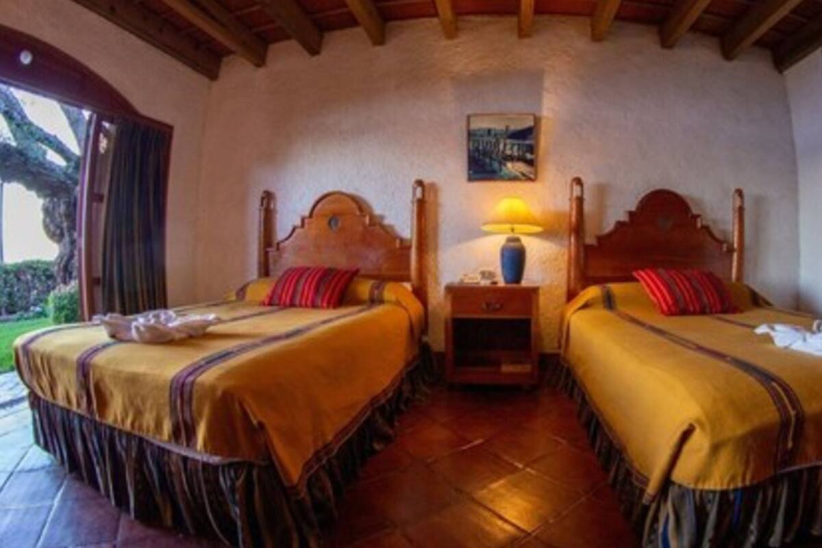 Quarto com duas camas, uma mesa de cabeceira com abajur e um quadro na parede.