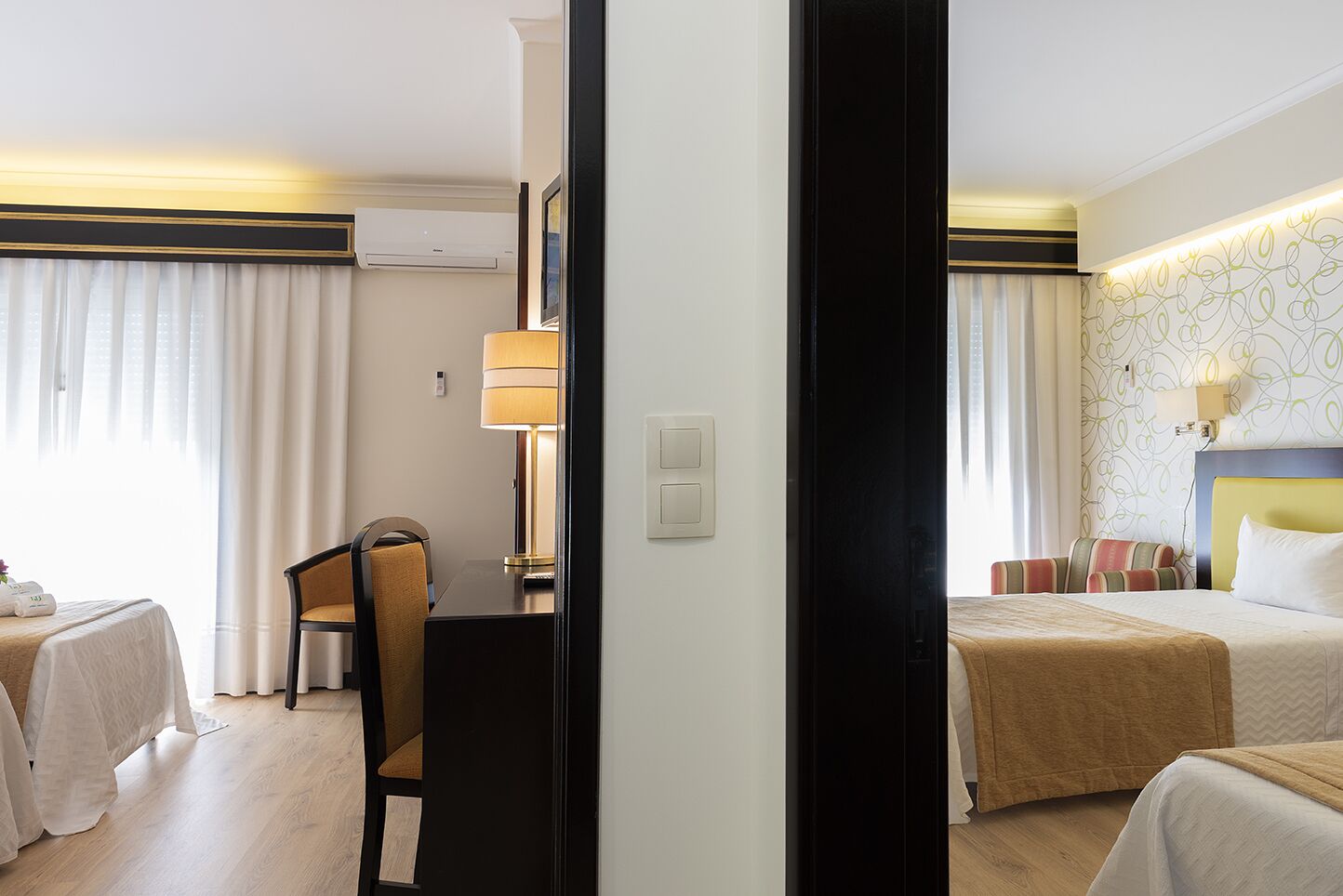 Quarto de hotel com duas camas, uma escrivaninha com cadeira, luminária e ar condicionado fixado na parede.