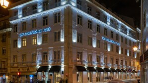 Hotel com vários andares, fachada iluminada, varandas e vista para a rua.