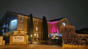 Entrada de um hotel com balcão de recepção, placa indicando o nome "HOTEL Lyon Sud" e entrada por portão.