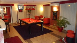 Uma mesa de bilhar em um espaço com cadeiras vermelhas, um relógio e um vaso de planta.