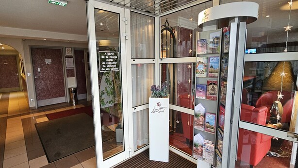 Um saguão de hotel com uma porta giratória, um balcão de recepção e uma exposição de folhetos de viagem.