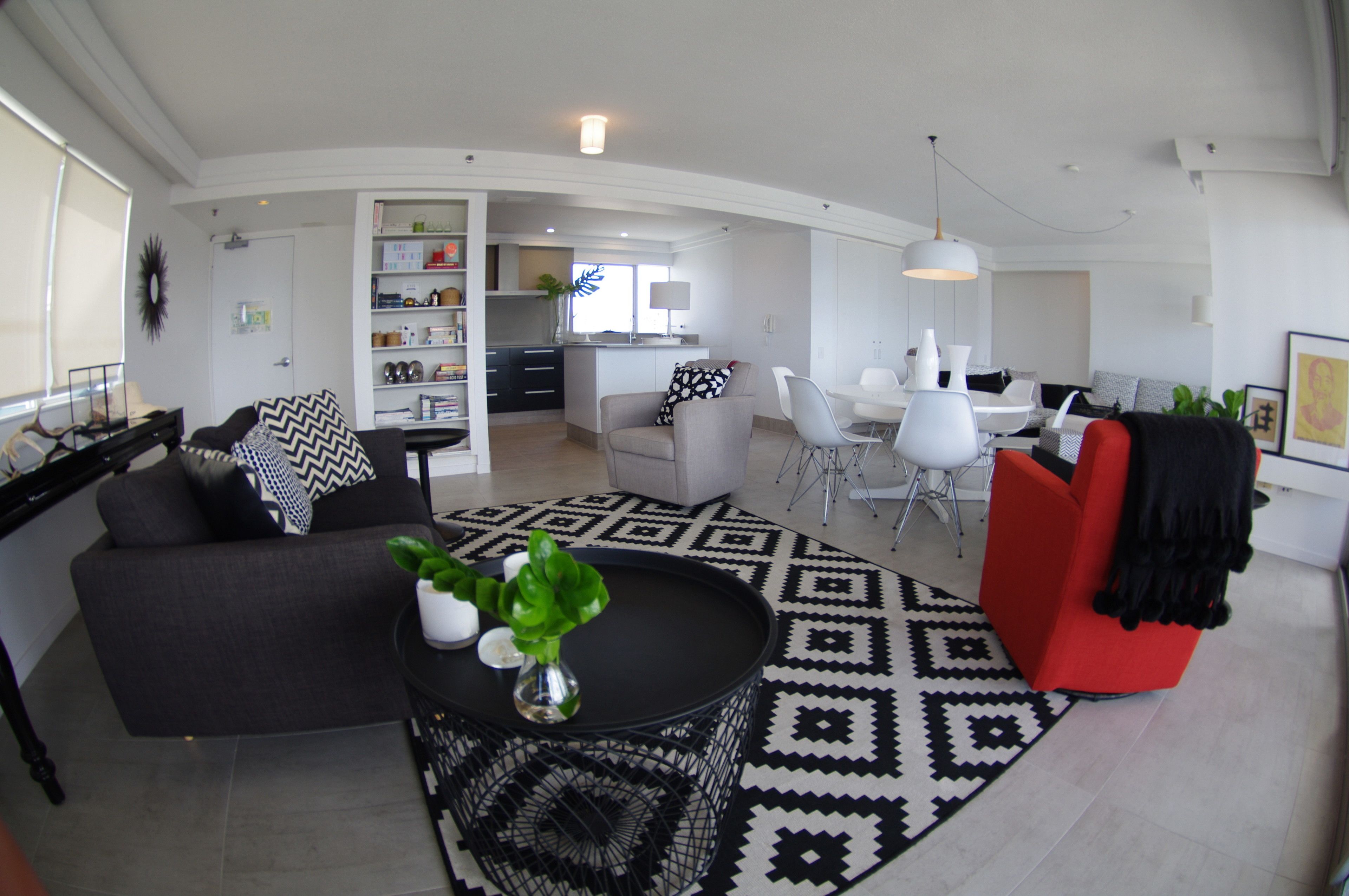 Uma sala de estar moderna com um sofá, uma mesa de centro com uma planta, um tapete estampado e uma cadeira vermelha.