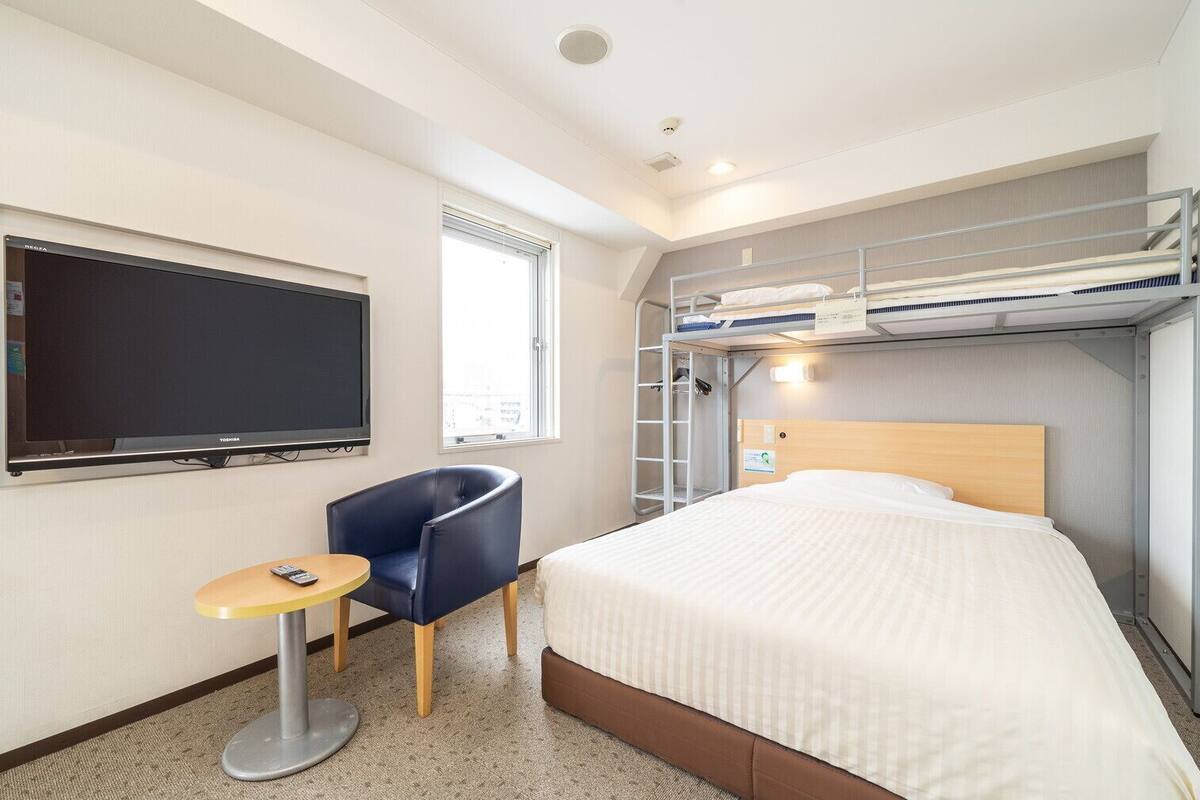 Quarto de hotel com uma cama, televisão, cadeira e mesa pequena.