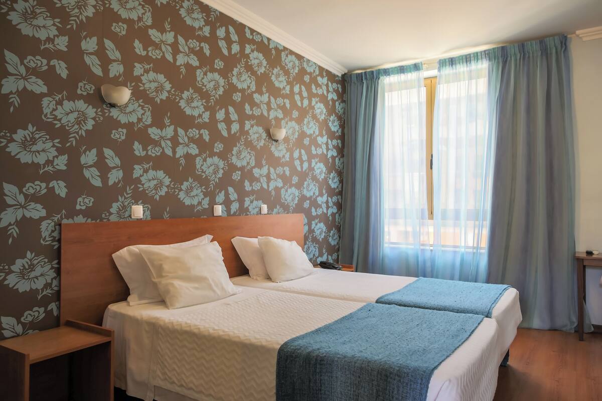 Uma cama de casal com cabeceira de madeira, duas almofadas brancas e um cobertor azul.