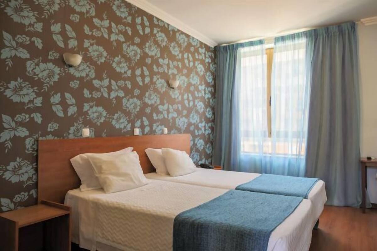 Cama de casal com cabeceira de madeira, duas mesas de cabeceira e papel de parede com padrão floral.