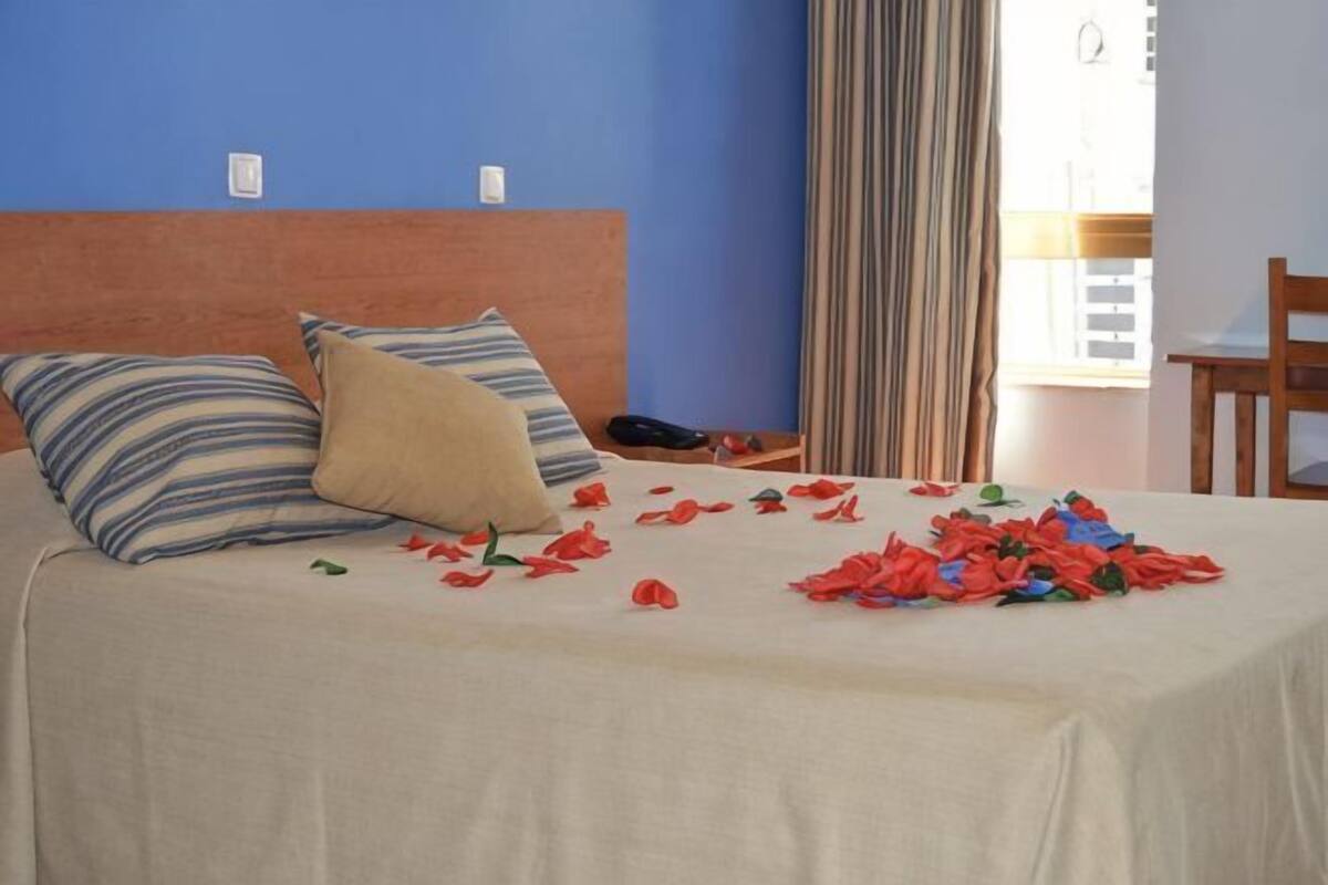Uma cama com cabeceira, almofadas e objetos espalhados.