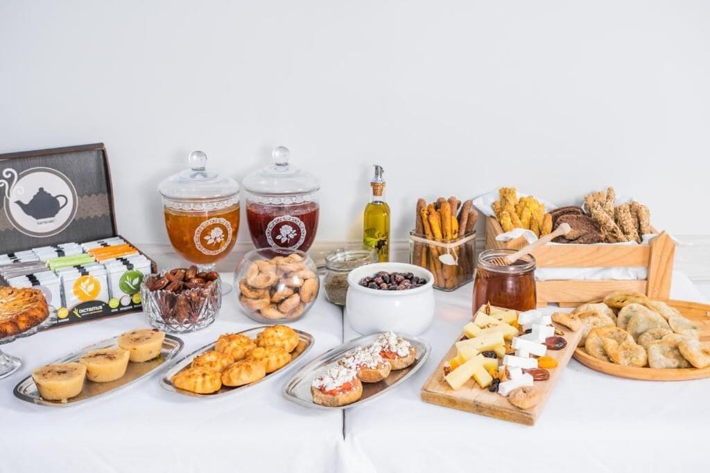 Diversos alimentos, incluindo potes de mel, potes de nozes, queijos e pães variados.