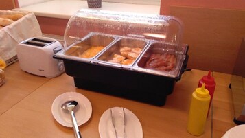 Buffet montado com torradeira, pratos e acompanhamentos.