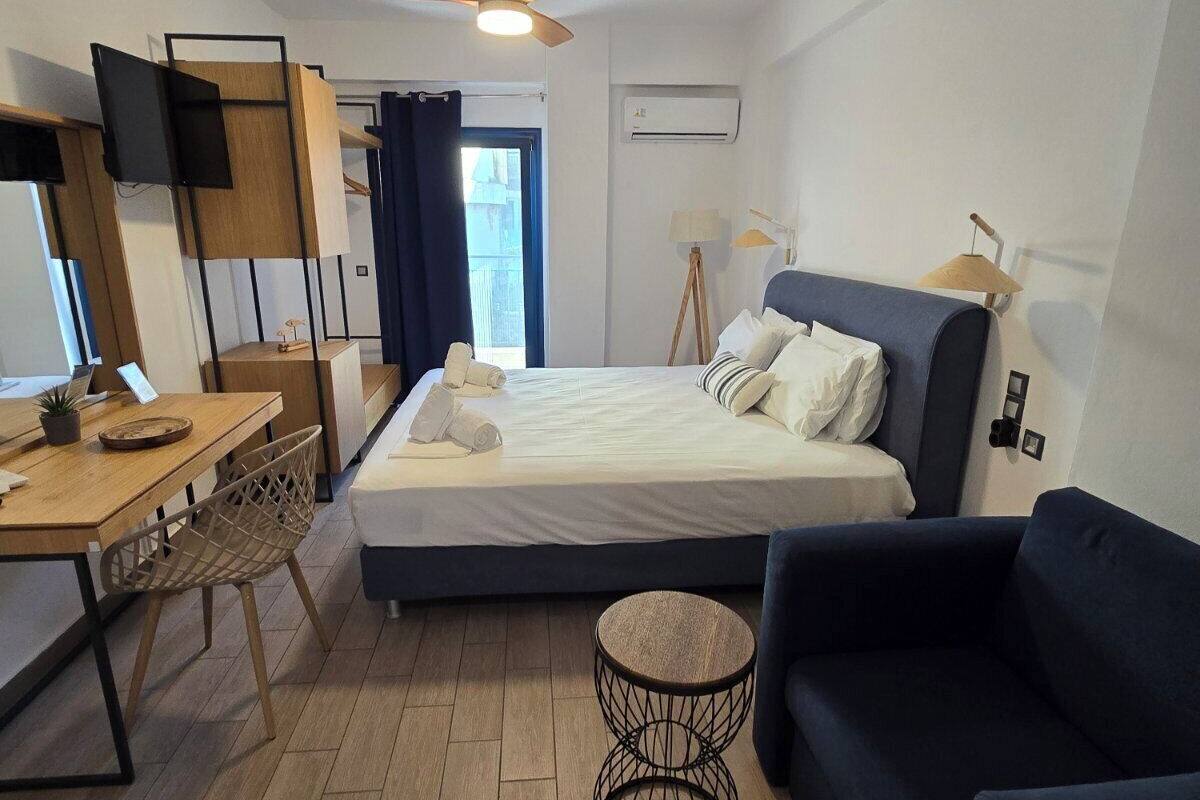 Quarto de hotel moderno com cama, escrivaninha, cadeira, mesa de canto redonda, sofá e ventilador de teto.