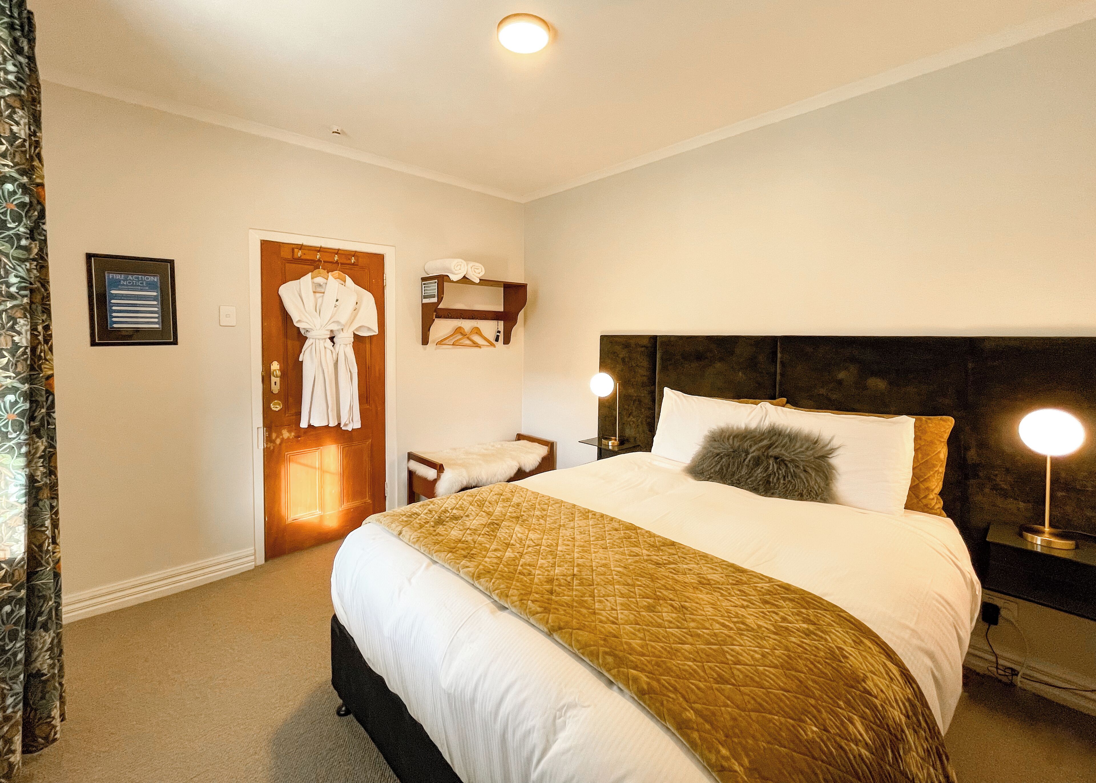 Quarto de hotel com uma cama grande, uma mesa de cabeceira, um roupão pendurado na porta e aviso de combate a incêndio.