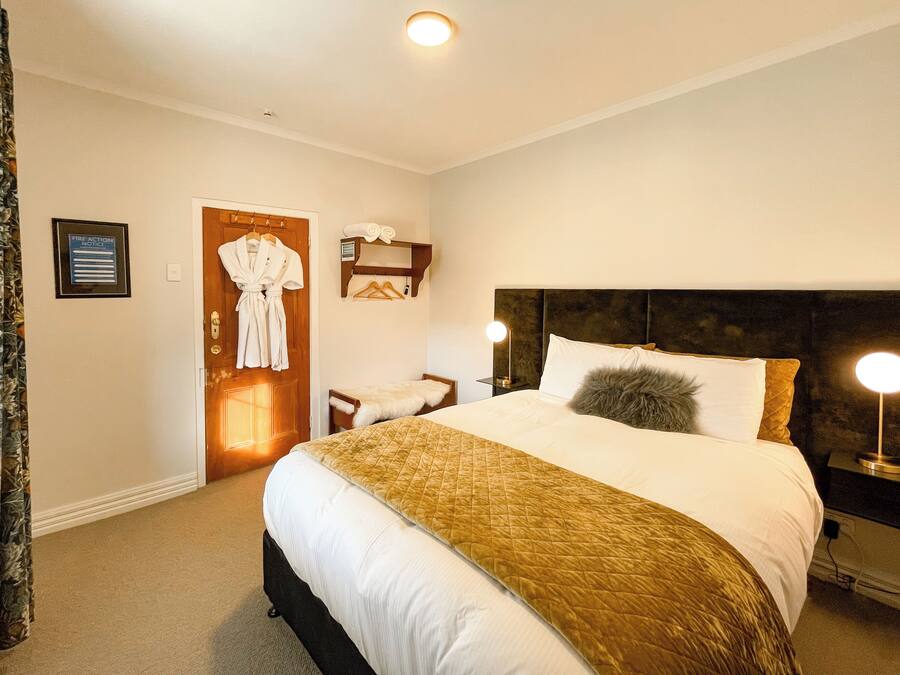 Quarto de hotel com uma cama grande, uma mesa de cabeceira, um roupão pendurado na porta e aviso de combate a incêndio.