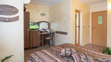 Quarto com cama, escrivaninha com computador, cadeira e televisão.