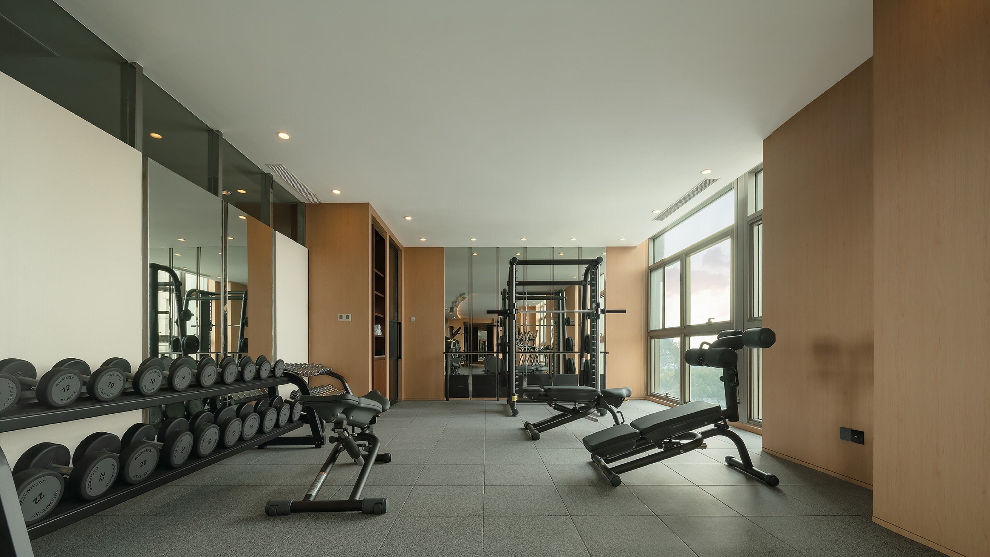 Uma academia moderna com equipamentos de musculação, espelhos e grandes janelas.